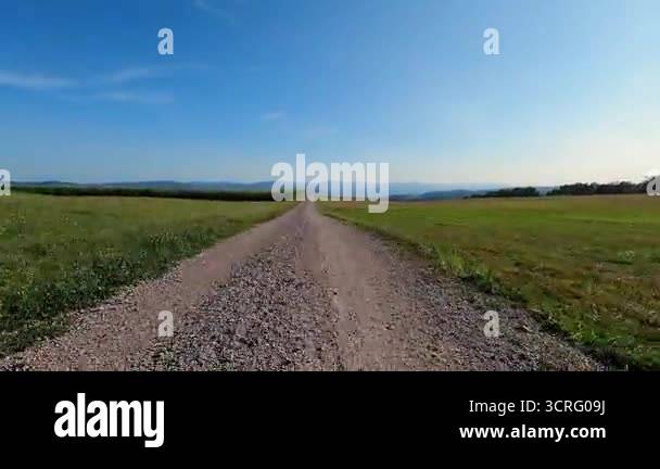 Riding on gravel dirt road along green agriculture fields and meadows ...