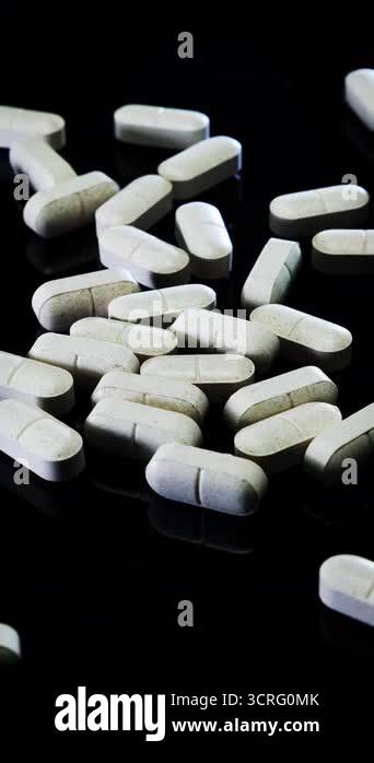 Pills and drugs rotating on black background. White tablets on table ...