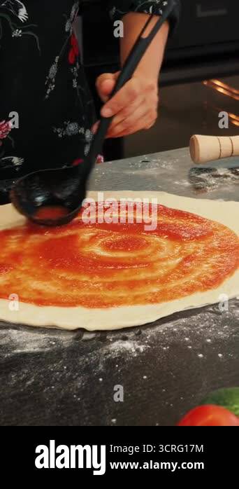 Woman spreading tomato sauce on pizza dough with ladle, making ...
