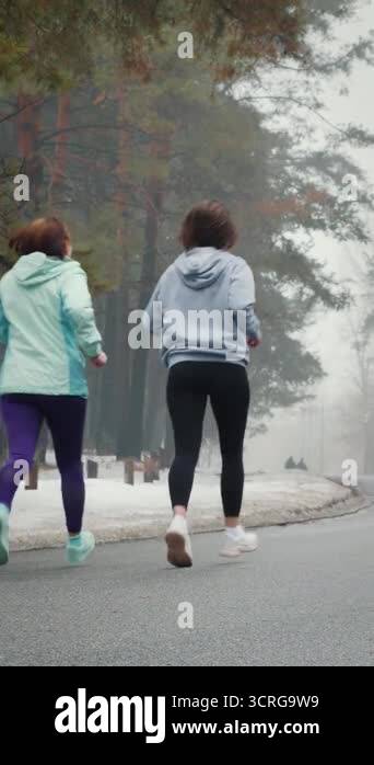 Two fit sportive females in sportswear running in snowy park in winter ...