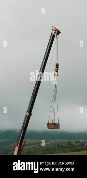 Working construction crane against foggy grey sky. Hook of elevating crane. Construction ...