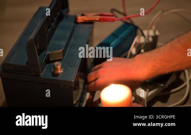 Charging gadgets from a battery by candlelight. A man connects an ...