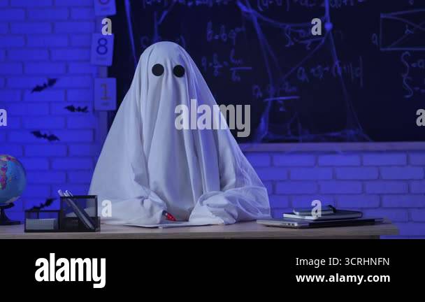 A man in a white ghost sheet sits at a table in a blue-lit room and ...