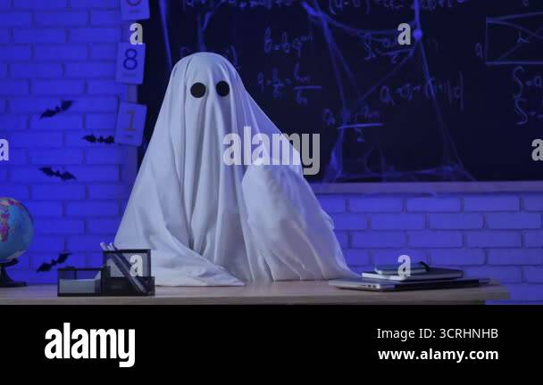 A person in a white ghost sheet sits at a table in a blue-lit room and ...