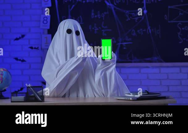 A person in a white ghost sheet shows a smartphone with a green screen ...