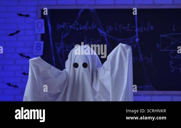 A person in a white ghost sheet scares students while sitting in a room ...