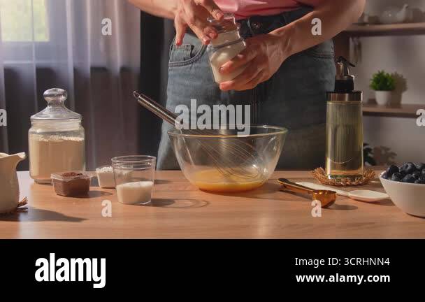 A woman measures and pours sugar into a glass bowl with beaten eggs and ...