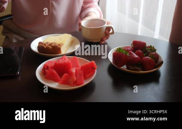 Unrecognizable woman having breakfast cheesecake tea fruit, hands close ...