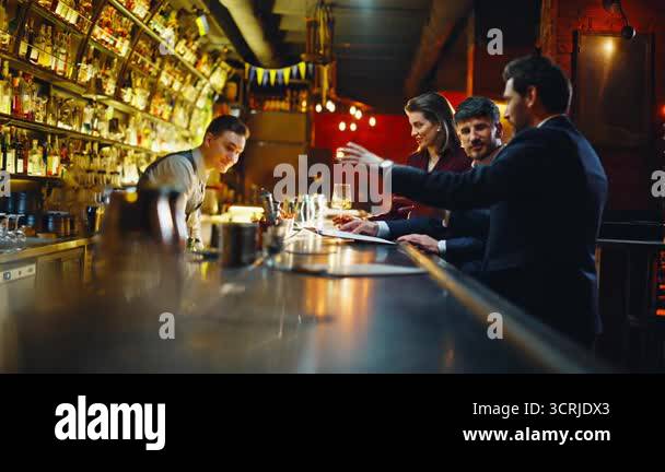 Happy businesspeople talking waiter ordering alcohol beverages at night ...
