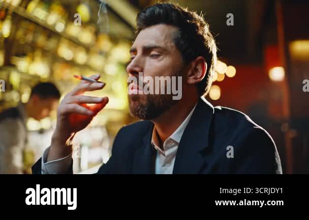 Pensive man inhaling smoke resting alone in silent lounge with dim ...