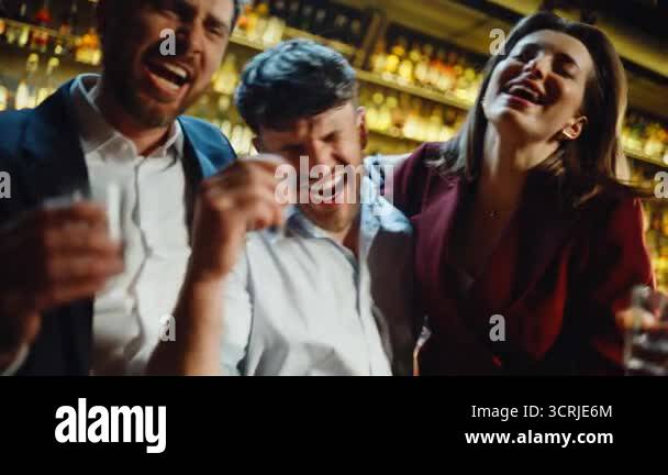 Drunk coworkers singing in bar holding shots in golden light place ...