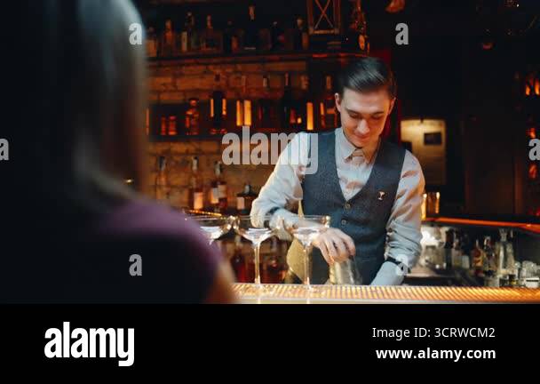 Friendly barkeeper mixing drinks beside glowing countertop in modern ...