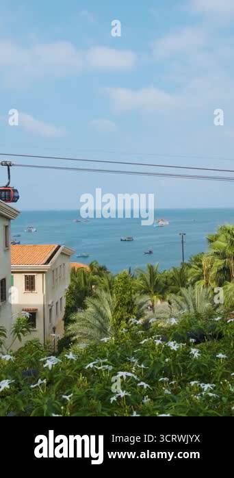 Modern cable car cabin ride over tropical seaside with fishing boats ...