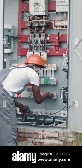 An electrician wearing a hard hat and safety glasses inspects an ...
