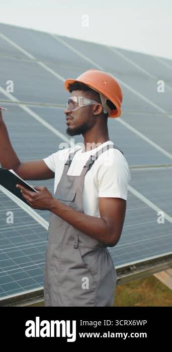 A technician in an orange hard hat inspects solar panels, ensuring ...