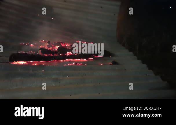 A smoldering fire on a corrugated metal roof. The glowing red embers ...