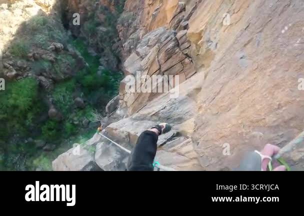 Cropped unrecognizable man climbs on a rocky cliff, with shoes, gloved hand grips climbing rope ...