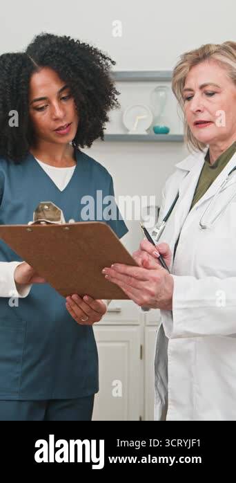 Medical professionals, a doctor and nurse, intently review patient documents on a clipboard ...