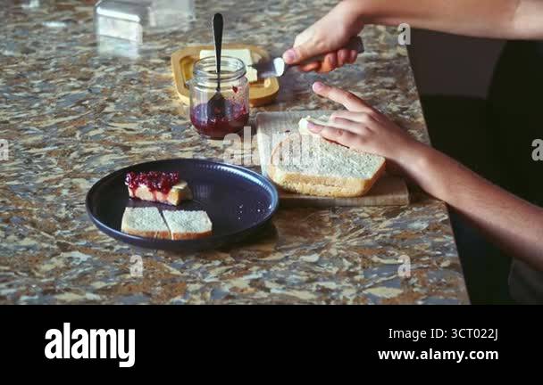 Side view of a boy at the kitchen table making a sandwich, cutting ...