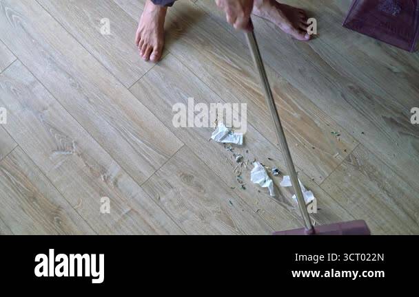 Medium shot lower body view of person sweeping trash on wooden floor ...