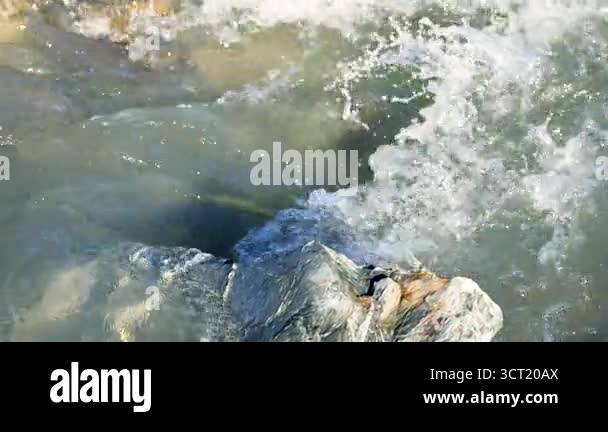 Clear water flows over rocks in a natural stream, creating dynamic ...