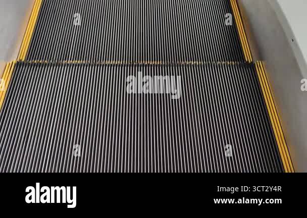 A close-up, high-angle view of empty escalator stairs moving down. The ...