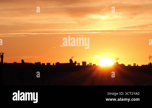 A vibrant sunset over a city skyline. The sun is low on the horizon ...