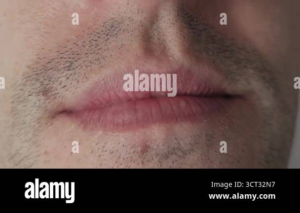 Macro shot of an unshaven mans lower face. He gives a slight, subtle ...