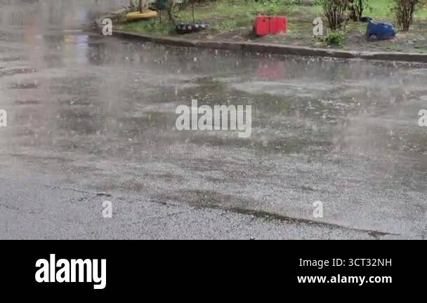 Raindrops splash onto a wet asphalt surface, creating ripples in ...