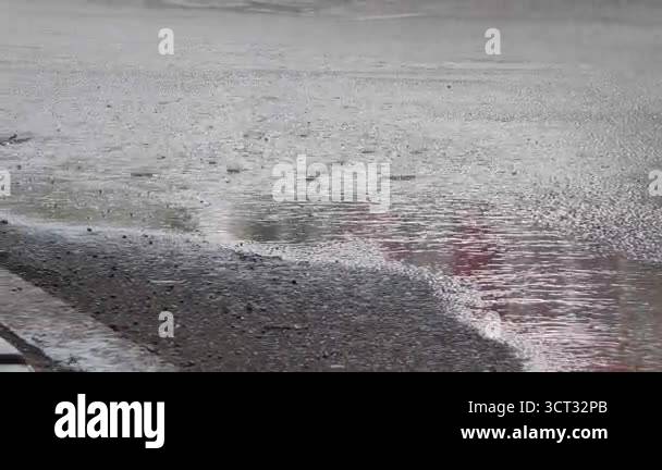 Heavy downpour on a city street as a car drives through a large puddle ...