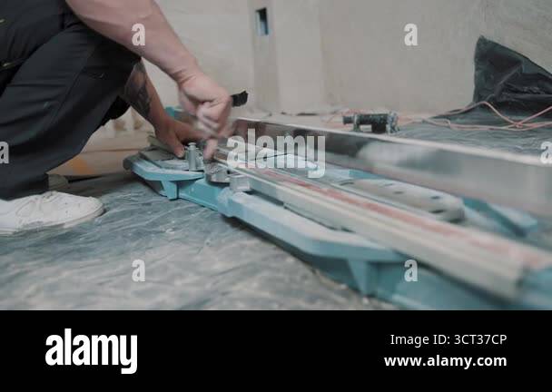 Man uses tile cutter tool to install floor tiles in a room during ...