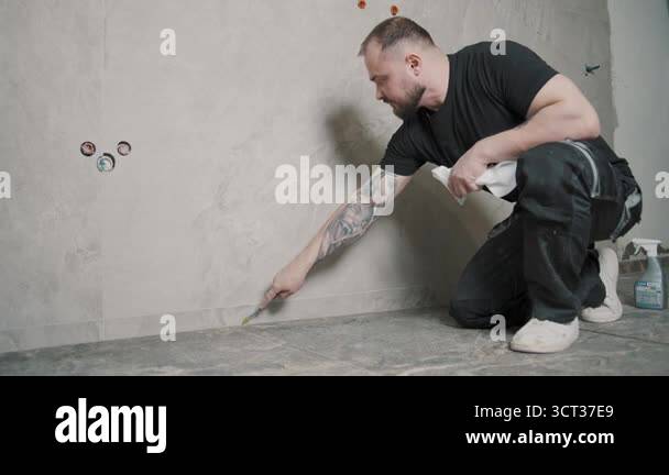 Man working on wall tiling using tools in a bright room during ...
