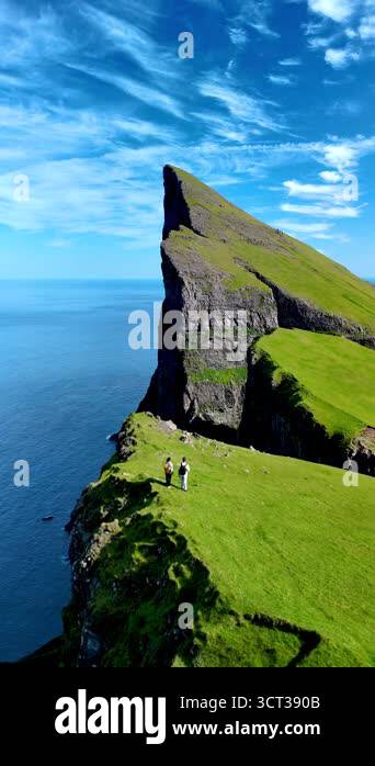 Explorers stand atop dramatic cliffs in the Faroe Islands, surrounded ...