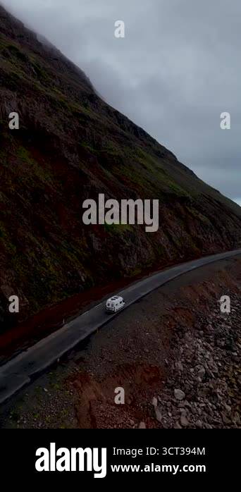 A lone camper van travels along a winding road in Iceland, surrounded ...
