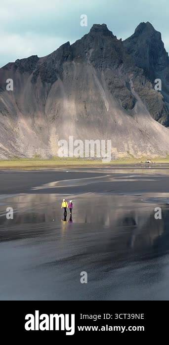 Two adventurers stand on a stunning black sand beach in Iceland ...