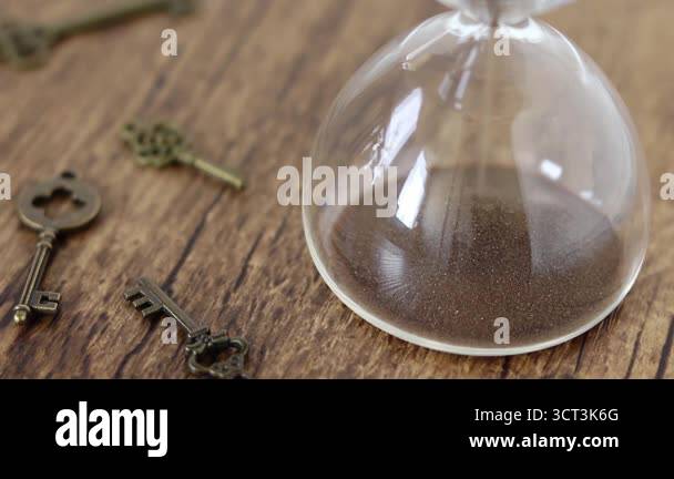 Hourglass with sand falling and ancient keys on wooden table. Close-up ...