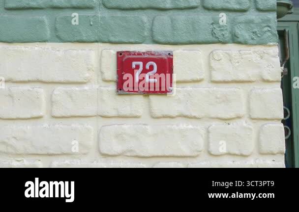 A bright red number sign is placed on a colorful wall made of bricks ...