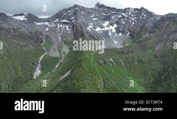An aerial video shows a lush, green mountain valley leading to a rocky ...