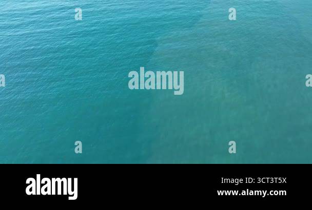 A top-down view of calm, clear turquoise ocean water with a subtle shift in color and texture ...