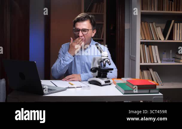 student, scientist at desk with microscope tired and yawning. Tired man ...