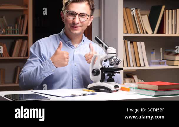Close-up portrait young scientist giving thumbs up while seated at desk ...