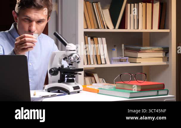 Close-up portrait scientist examining a sample slide under a microscope in a lab, surrounded by ...