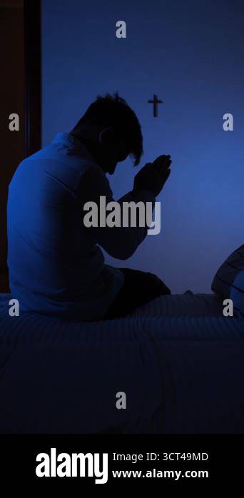vertical video Man kneeling in his bedroom at night, praying with ...