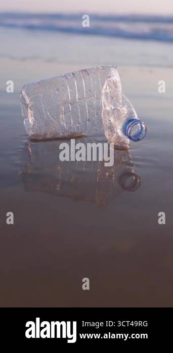vertical shot. Slow motion Ocean waves are washing plastic bottles from ...