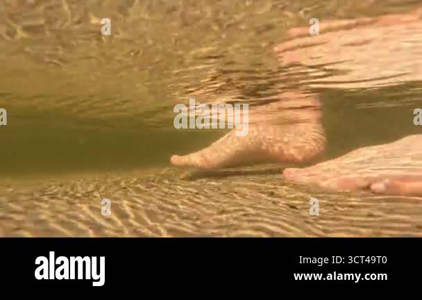 Underwater view capturing feet standing on the sandy bottom of a murky ...