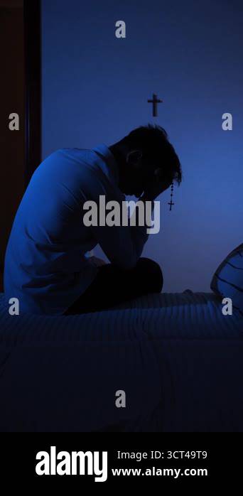 vertical video christian Man sitting on a bed in a dark room at night ...