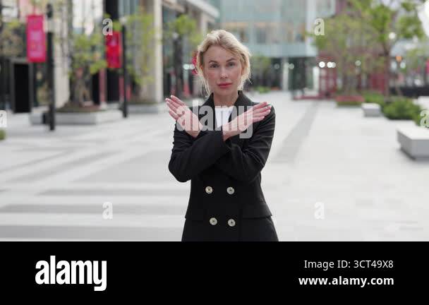Portrait of woman manager shows Cancel gesture near downtown buildings ...