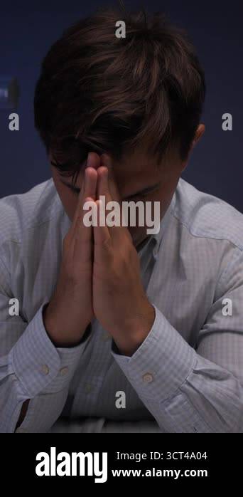 vertical video Man praying with his hands clasped together, head bowed ...