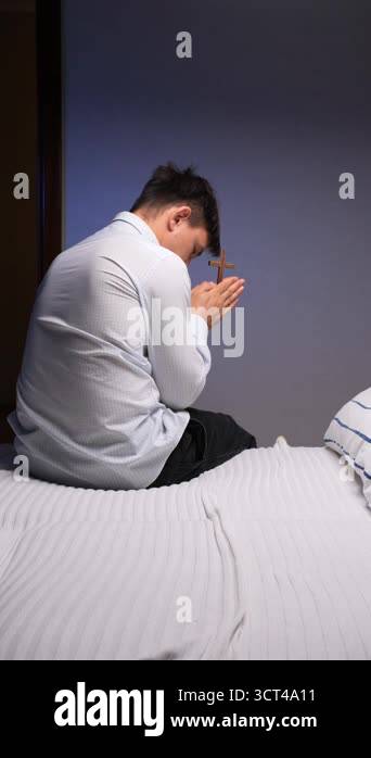 vertical video Young man sitting on his bed, holding a small wooden ...