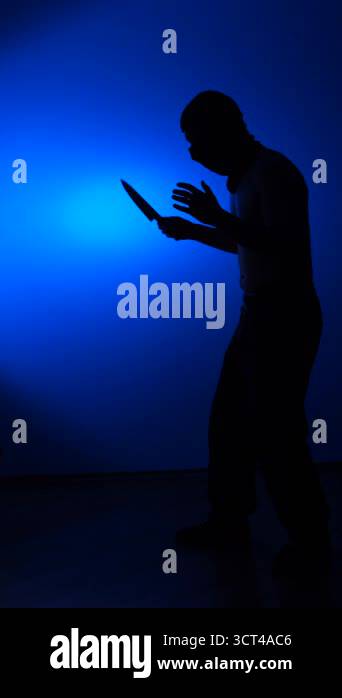 vertical video Silhouetted man holding a knife in dramatic blue light ...